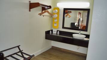 Casa de banho com bancada preta, lavatório branco, espelho e suporte de madeira para cabides.