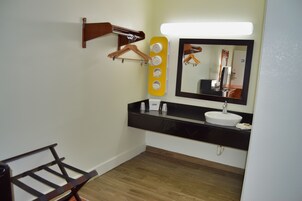 Casa de banho com bancada preta, lavatório branco, espelho e suporte de madeira para cabides.