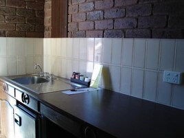 Uma cozinha com uma pia de aço inoxidável, forno embutido e parede de tijolos.