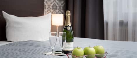Uma cama com uma garrafa de champanhe Veuve Clicquot, duas taças e três maçãs verdes sobre uma bandeja.