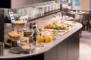 Buffet com diversos alimentos e bebidas, incluindo uma barra de saladas e uma exposição de frutas.