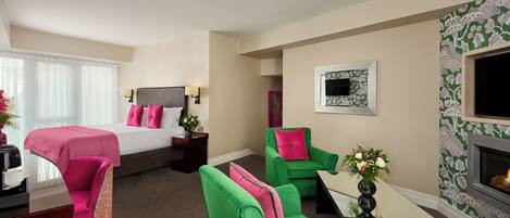 Quarto de hotel com cama, duas poltronas verdes, mesa de centro, televisão e lareira.