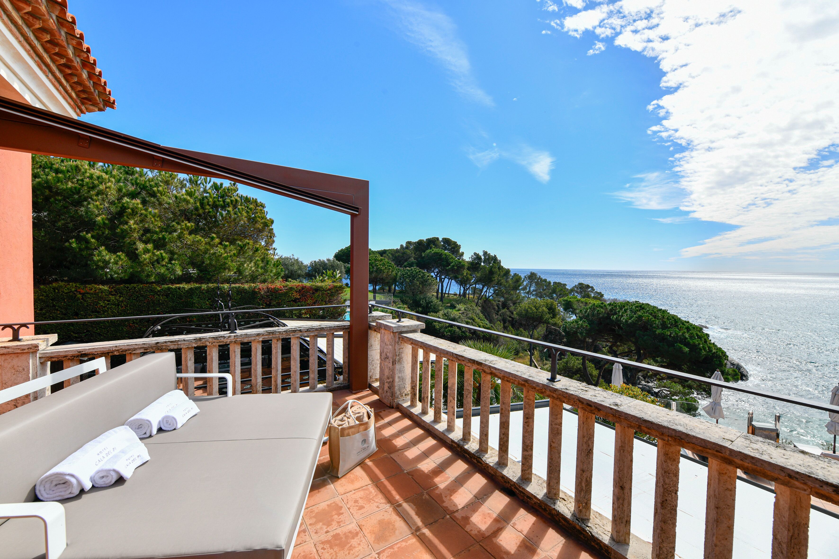 Varanda com vista para o mar, um sofá branco e uma mesa com toalhas enroladas.