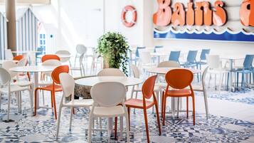 Interior de restaurante com mesas e cadeiras redondas, piso estampado e um letreiro com a inscrição 'Bains'.