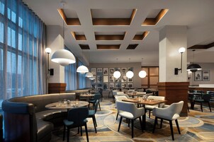 Um restaurante moderno com área de estar curvada, várias mesas de jantar e iluminação pendente.