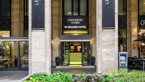 Entrada do Hotel M-Square com uma placa chamativa, área de estar ao ar livre e um caixa eletrônico.