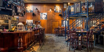 Uma área de bar com painéis de madeira, banquetas e uma escada com corrimãos azuis.