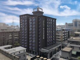 Um edifício alto com a fachada identificada pelo nome 'Mercure Hotel', apresentando um design arquitetônico moderno com várias janelas e sacadas.