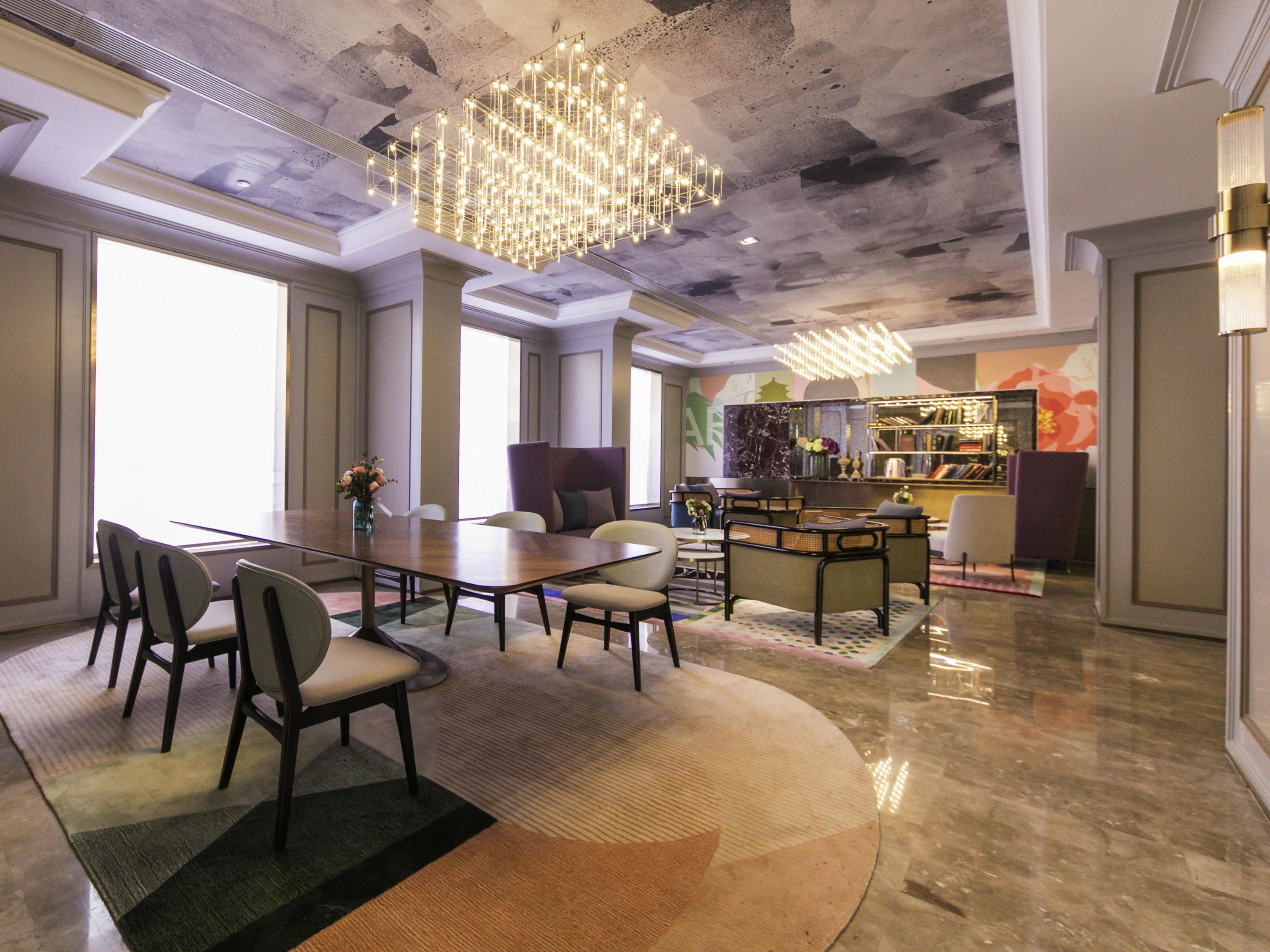 Um hall de hotel moderno com uma grande mesa de jantar, assentos confortáveis, um espaço de bar e um design de teto único.
