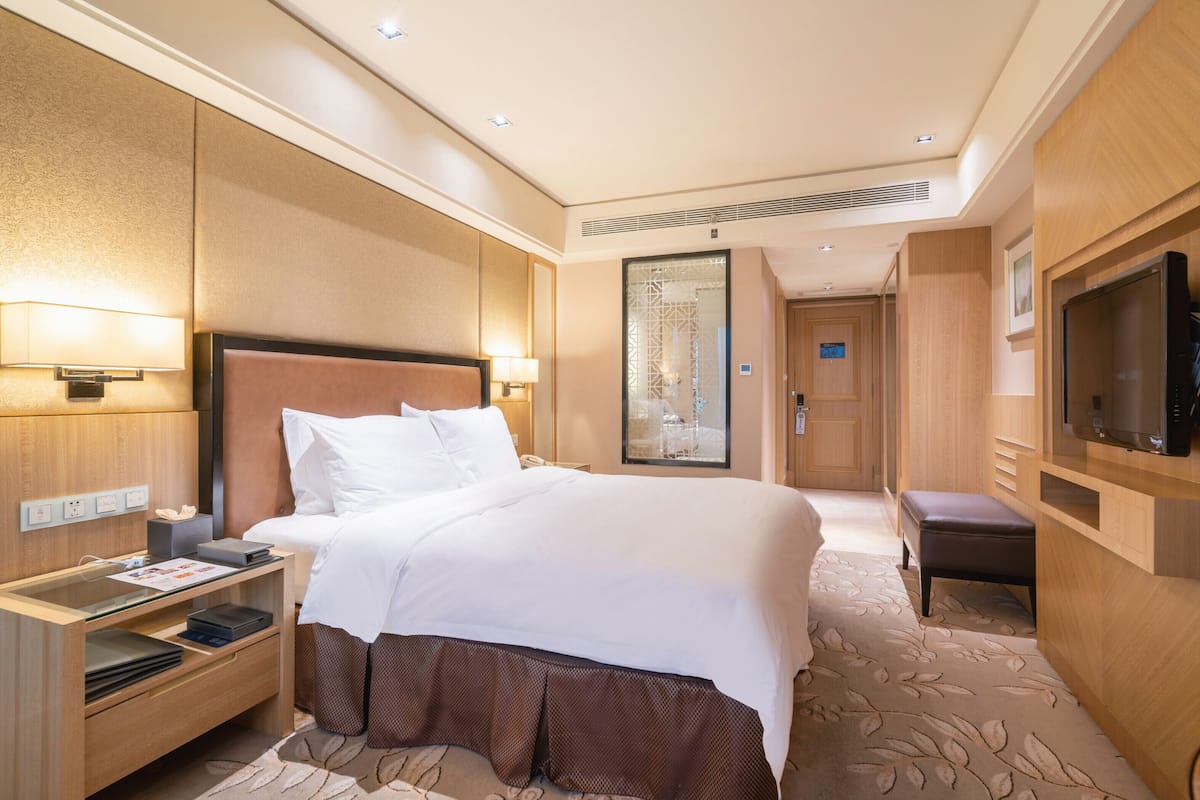 Quarto de hotel com uma cama grande, mesas de cabeceira, televisão e closet espaçoso.