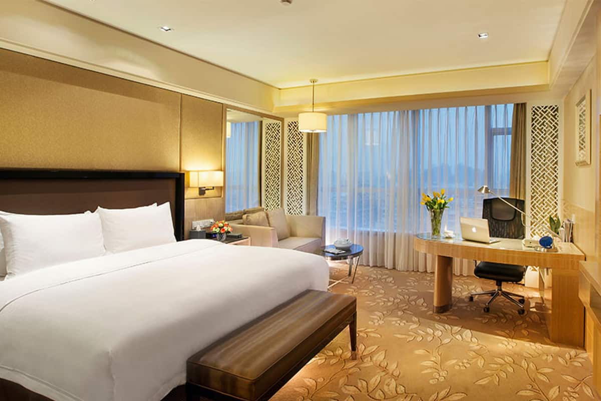 Quarto de hotel com uma cama grande, uma escrivaninha, uma cadeira, um laptop e vista para a cidade pela janela.