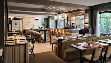 Um restaurante moderno com área de bar, pé direito alto e grandes janelas.