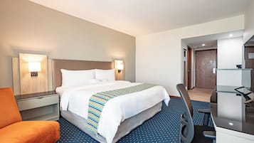 Quarto de hotel com cama, escrivaninha, cadeira e mesa de cabeceira.