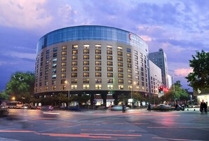 Um hotel com fachada de vidro curvo, vários andares e uma entrada destacada.