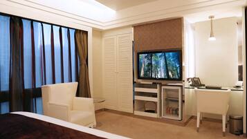 Quarto de hotel com cama, televisão, secretária e cadeira.