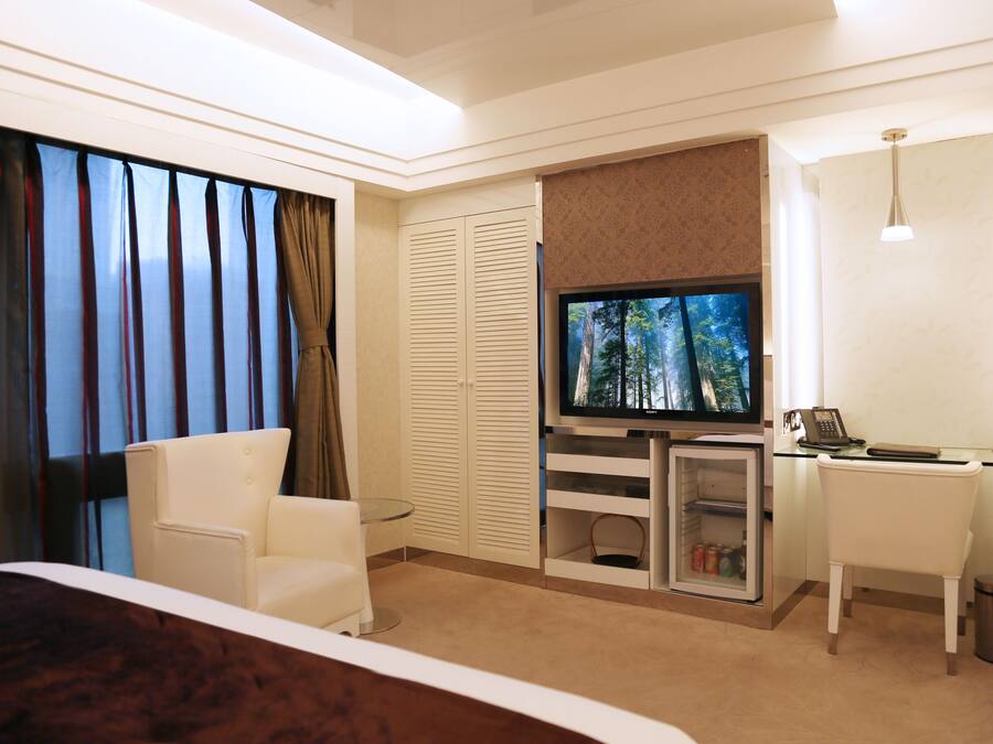 Quarto de hotel com cama, televisão, secretária e cadeira.