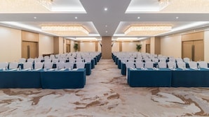 Uma sala de conferências com fileiras de mesas e cadeiras, carpete estampado e luminárias decorativas.