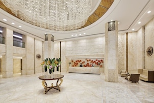 Um hall amplo com piso de mármore, um balcão de recepção e um grande candelabro.