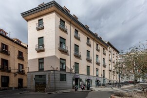 Um edifício de vários andares com varandas, entrada com portão e loja com letreiros.