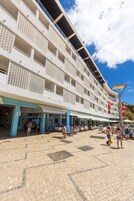 Um hotel com vários andares, área externa coberta, mesas ao ar livre e uma piscina.
