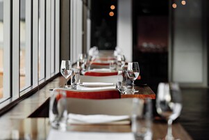 Restaurante com uma mesa comprida posta para refeição, apresentando um design moderno com mesa de madeira e cadeiras de metal.