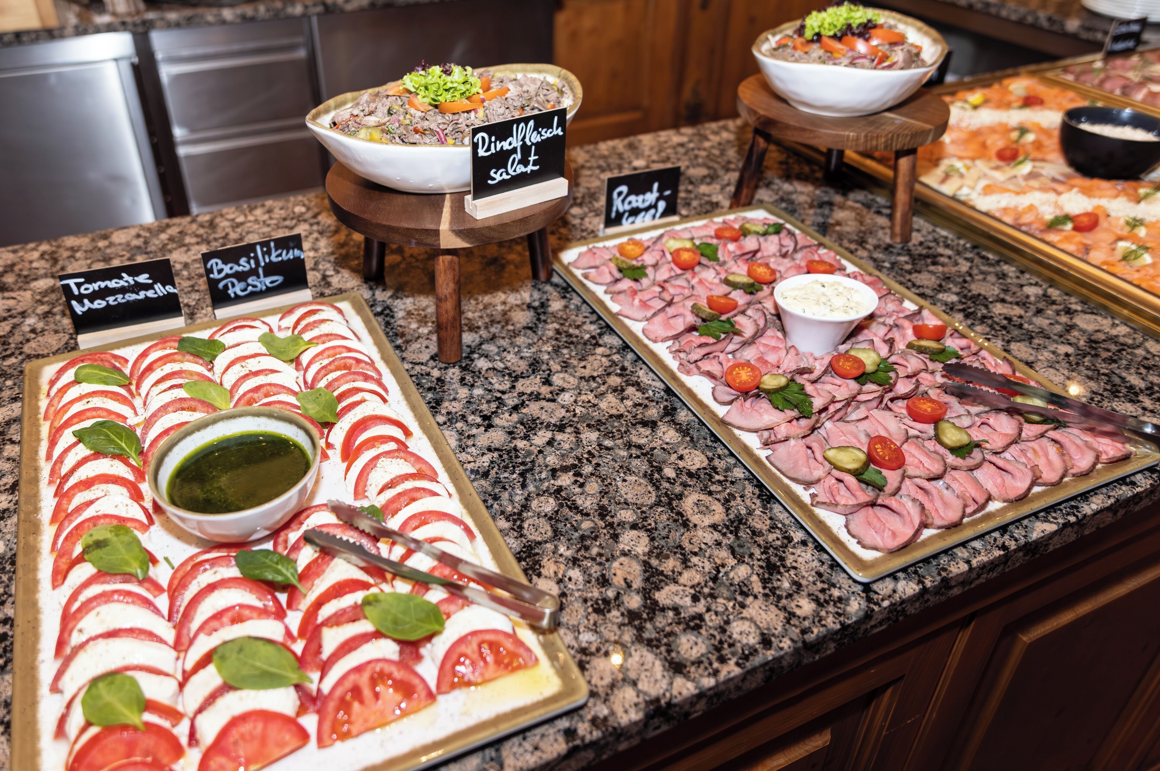 Buffet com diversas opções de comida, incluindo tomate e mussarela, pesto de manjericão e rosbife.