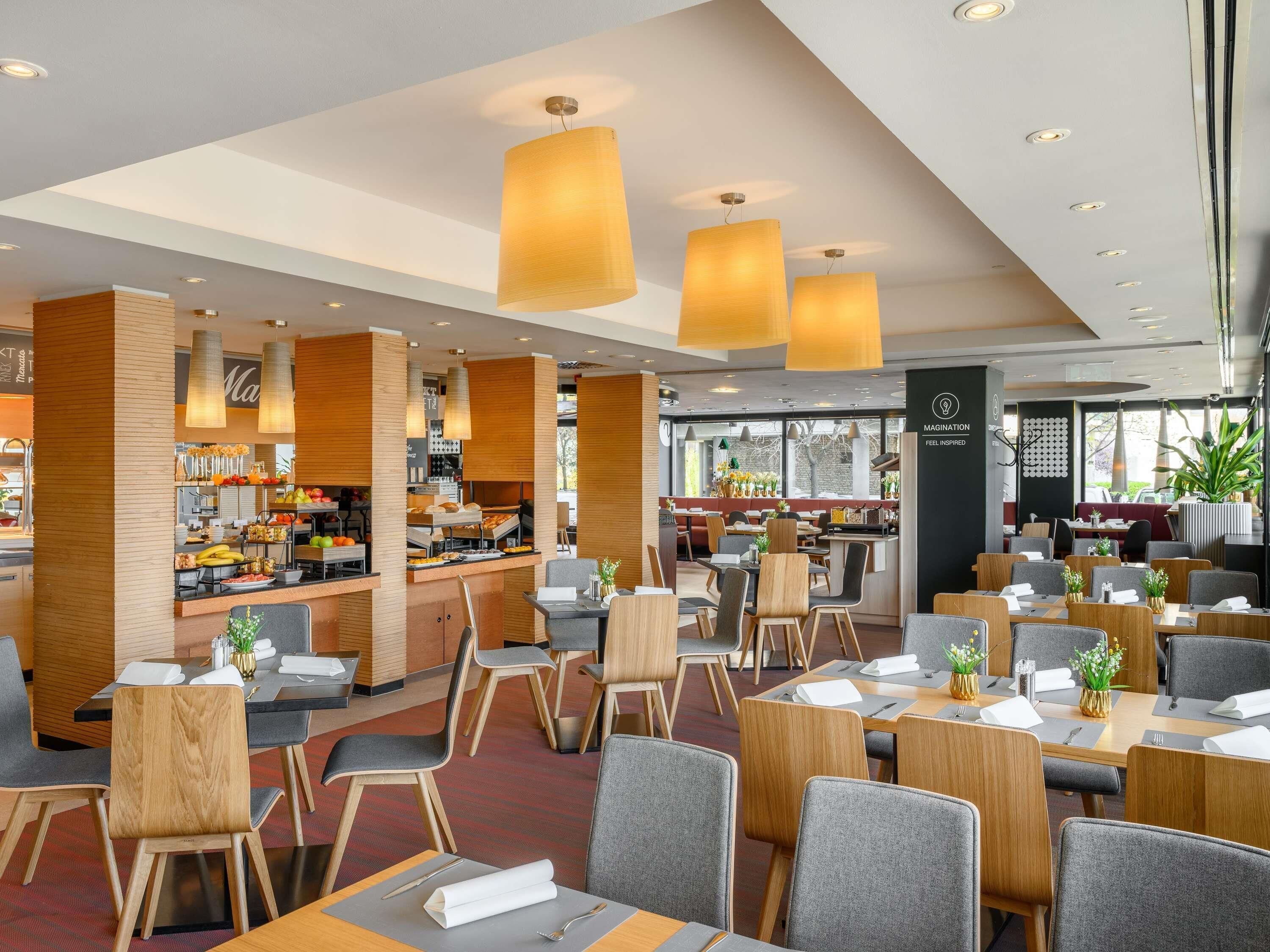 Restaurante moderno com detalhes em madeira, espaço para buffet e área de refeições com mesas e cadeiras.