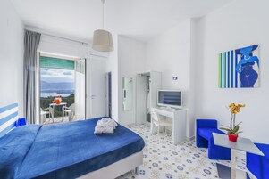 Quarto de hotel com cama, escrivaninha, televisão e varanda com vista.