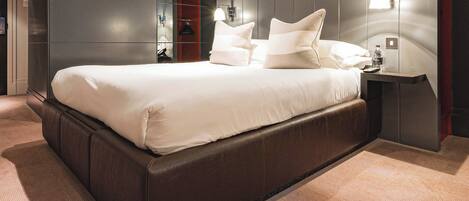 Quarto de hotel moderno com uma cama grande, uma mesa de cabeceira com abajur e um espelho na parede.