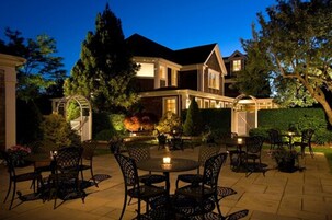 Uma casa grande com um pátio, mobiliário de exterior e um jardim bem iluminado.