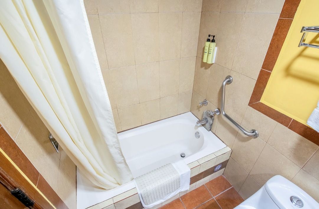 Um banheiro com banheira, barras de apoio, vaso sanitário e porta-toalhas.