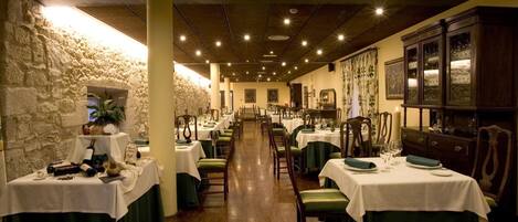 Um restaurante com mesas preparadas para refeições, uma parede de pedra de um lado e um armário de madeira do outro.