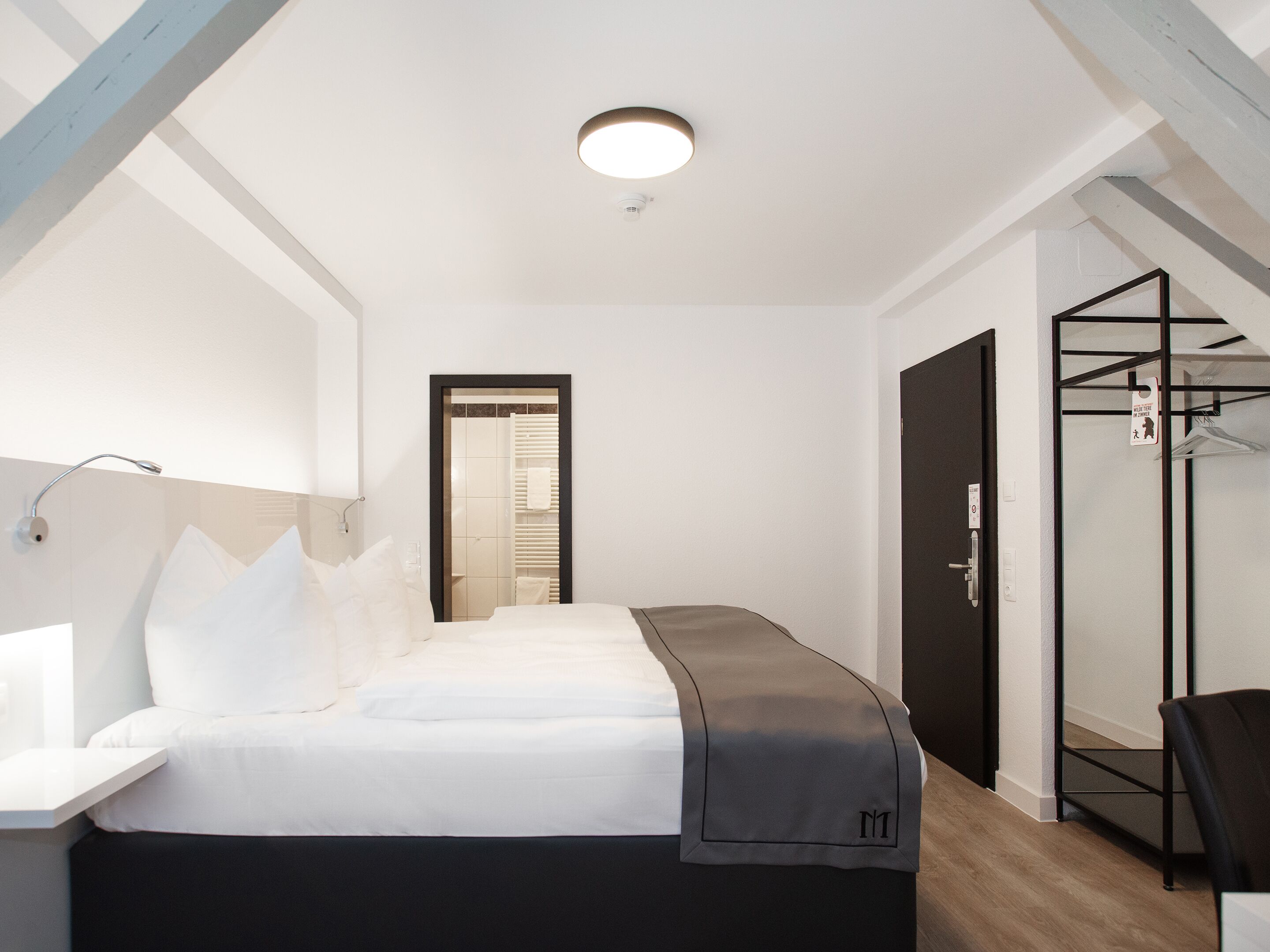 Quarto de hotel moderno com cama, escrivaninha, cadeira, closet espaçoso e área de chuveiro.