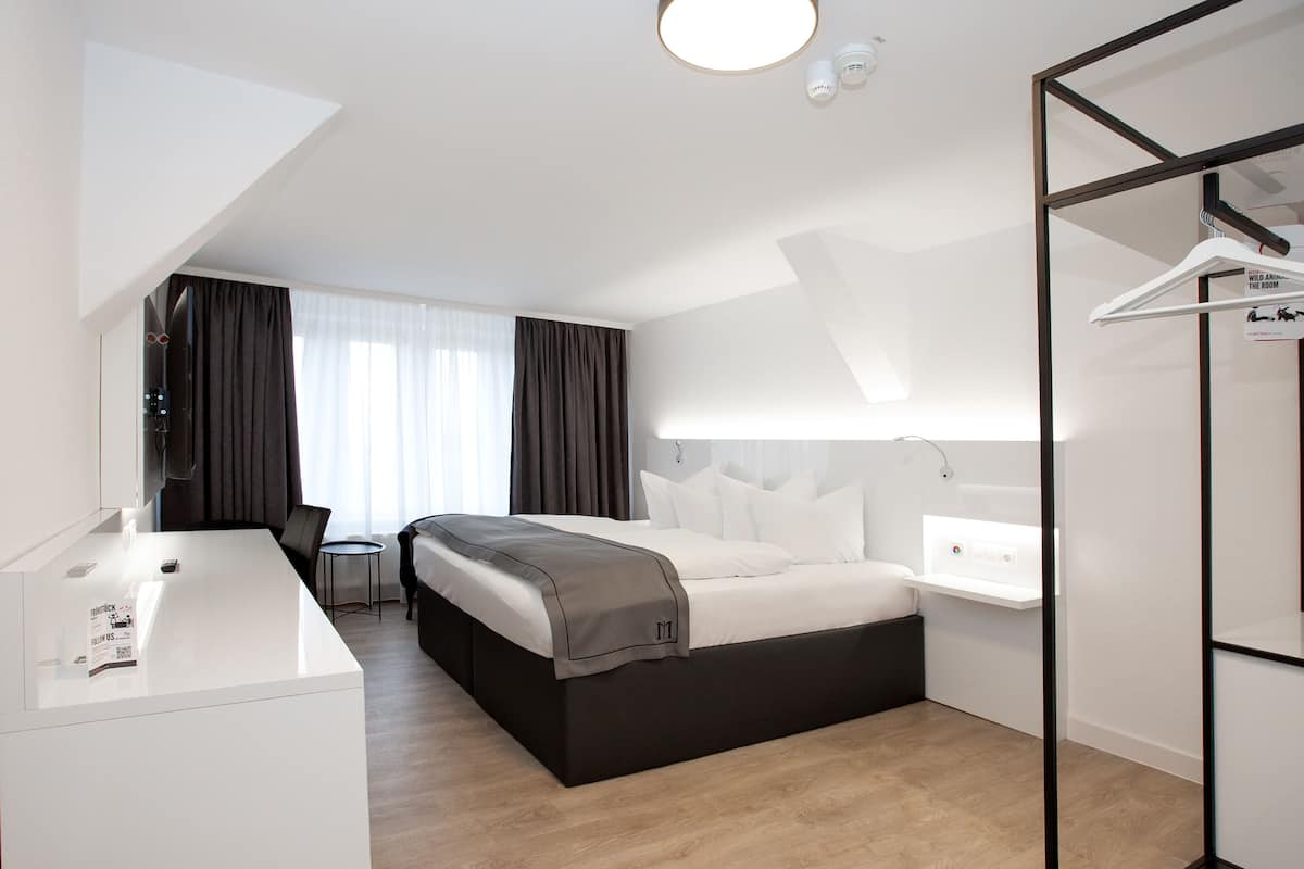 Quarto de hotel moderno com cama, mesas de cabeceira, escrivaninha e espelho.