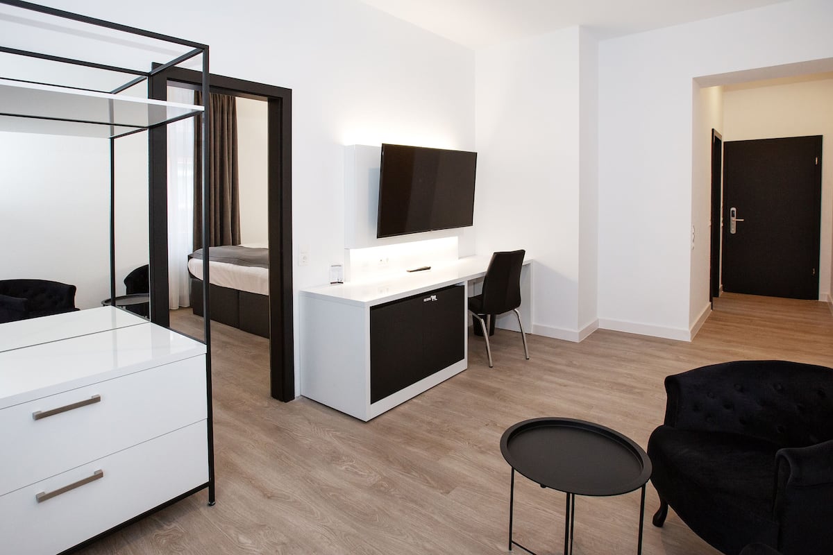 Quarto de hotel moderno com escrivaninha branca, cadeira preta e um espelho grande.