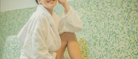 Uma pessoa sentada num banco revestido de mosaico verde num espaço com parede igualmente revestida de azulejos verdes.