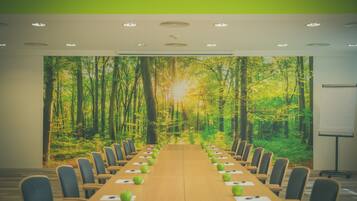 Uma sala de conferências com uma mesa comprida, cadeiras e um mural com tema de floresta na parede.