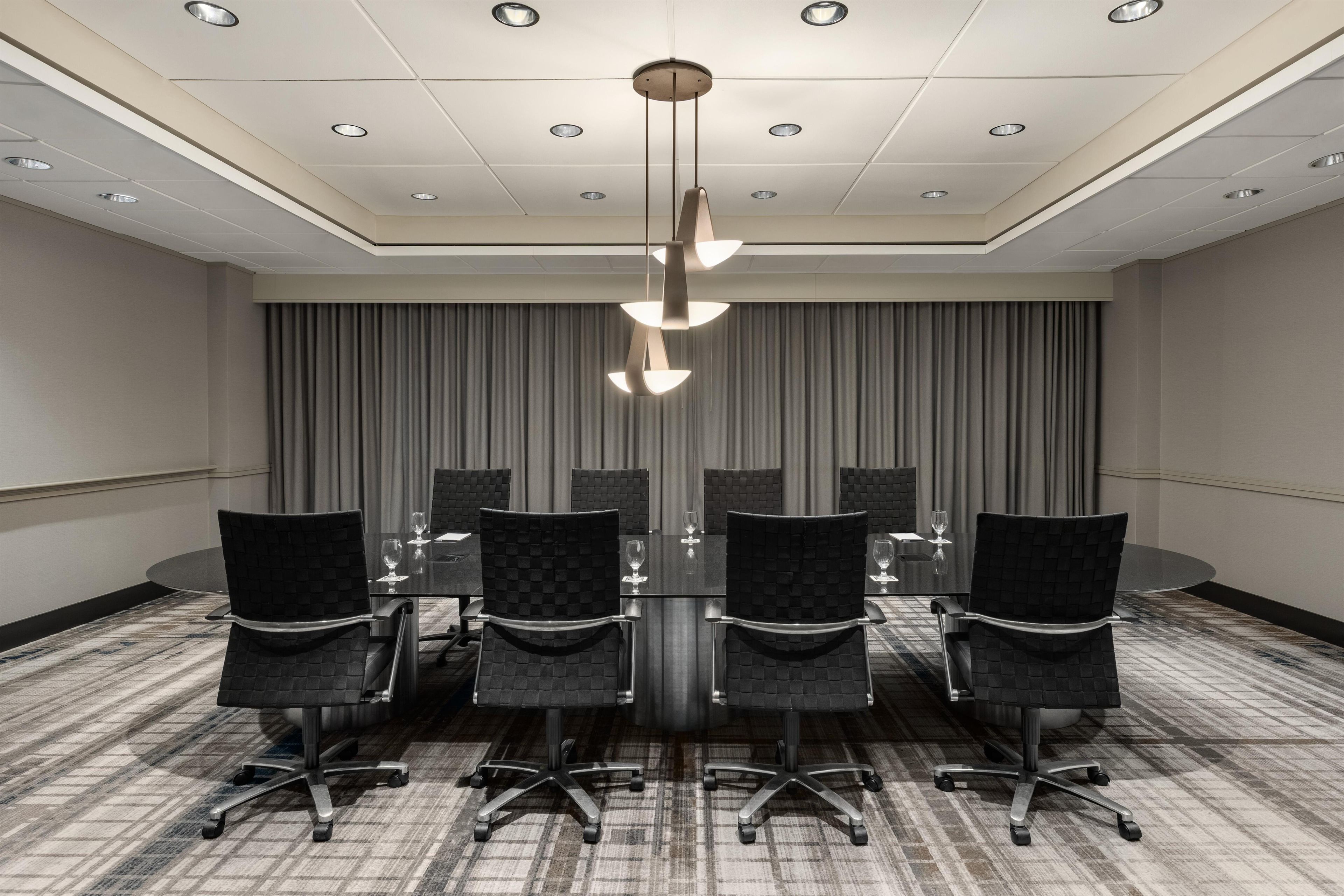 Uma sala de conferências com uma mesa retangular, seis cadeiras e um lustre moderno.