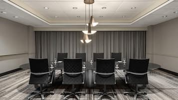 Uma sala de conferências com uma mesa retangular, seis cadeiras e um lustre moderno.