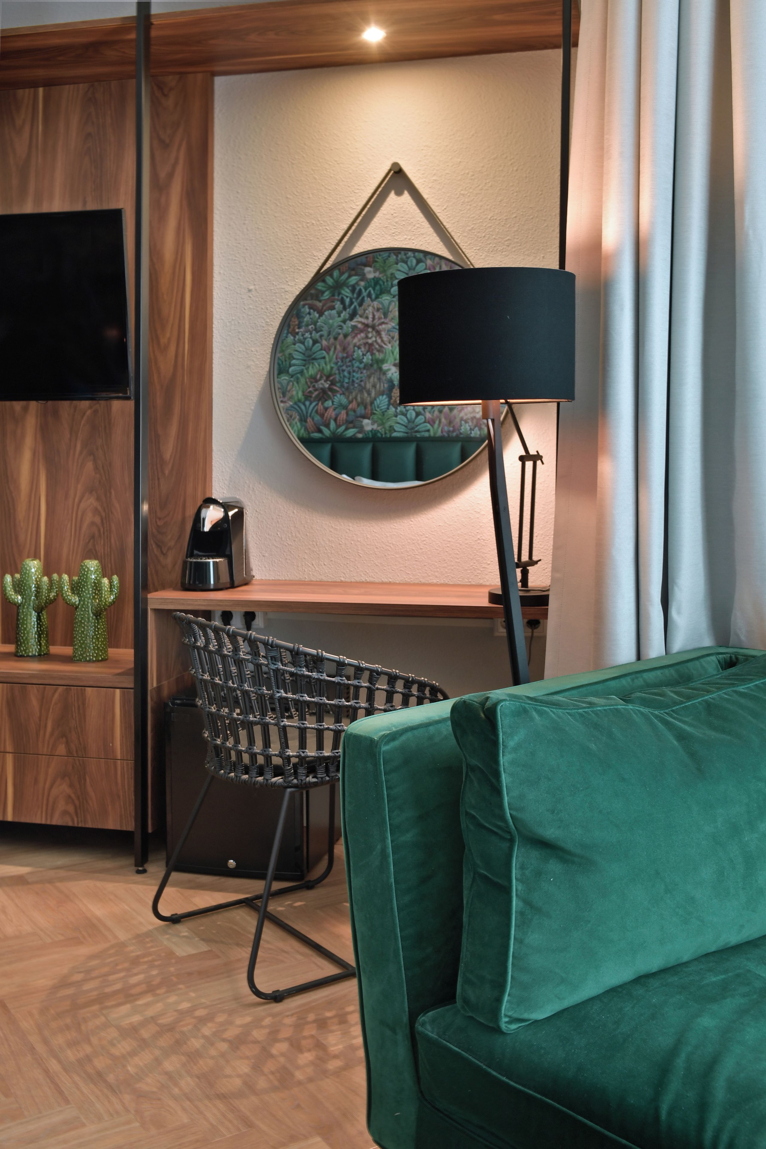 Quarto moderno com escrivaninha de madeira, sofá verde, espelho redondo e luminária.