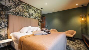 Quarto de hotel com uma cama grande, uma cadeira, uma mesa de cabeceira e parede com papel de parede tropical.