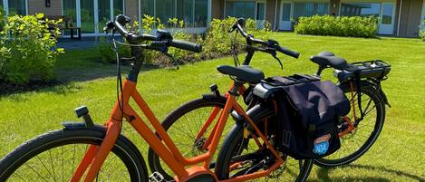 Bicicleta com uma bolsa preta, estacionada em área gramada em frente a um edifício com várias janelas e sacadas.