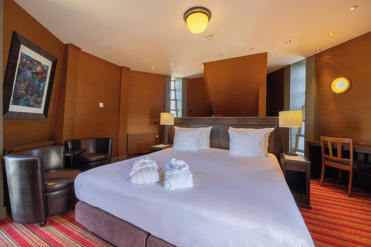 Quarto de hotel com uma cama grande, duas poltronas, uma escrivaninha e uma cadeira.