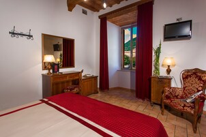 Quarto com cama, cômoda, cadeira, televisão e janela com cortinas.