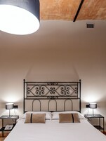 Uma cama bem arrumada com cabeceira, duas mesas de cabeceira com abajures e um lustre no teto.