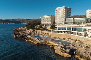Um hotel à beira-mar com piscina, várias varandas e vista para o mar.