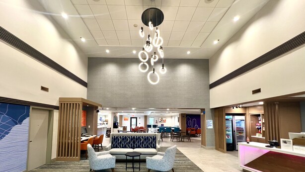 Um hall amplo com área de estar central, balcão de recepção e um espaço para alimentação.
