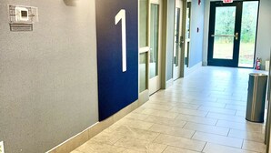 Corredor com placa de número '1', sinalização de saída e um cesto de lixo.