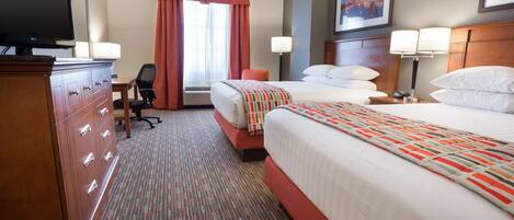 Quarto de hotel com cama, escrivaninha, cadeira, televisão e um quadro na parede.