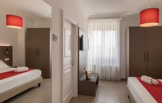 Quarto de hotel com duas camas, televisão, minibar e uma grande janela com cortinas.